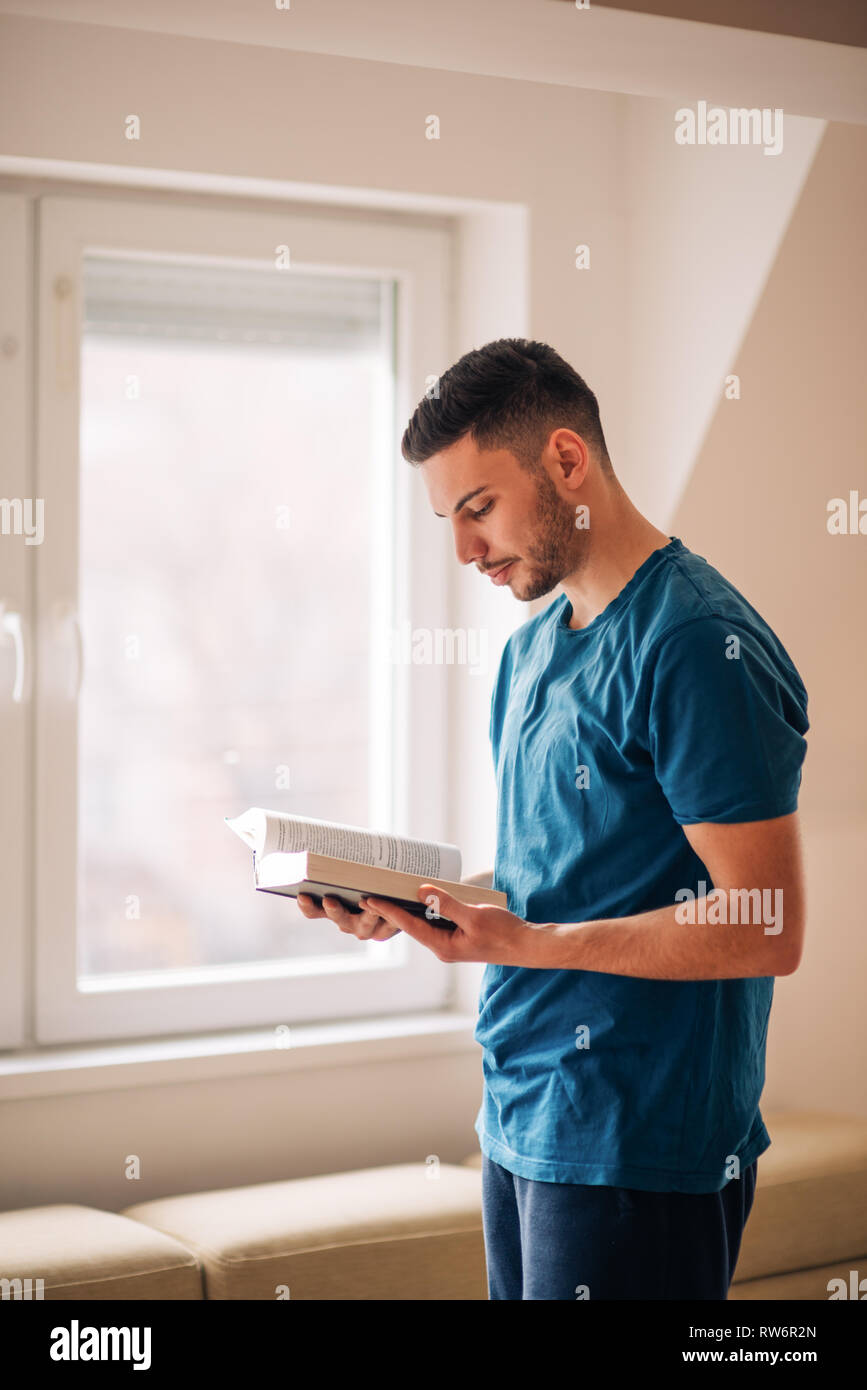 Student reading a book while standing and walking in the room next to ...