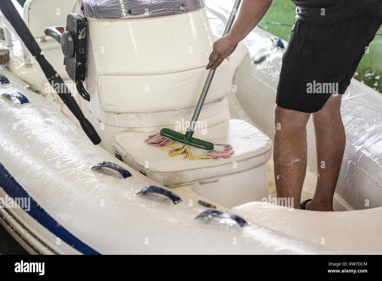 Man washing white inflatable boat with brush and pressure water system ...