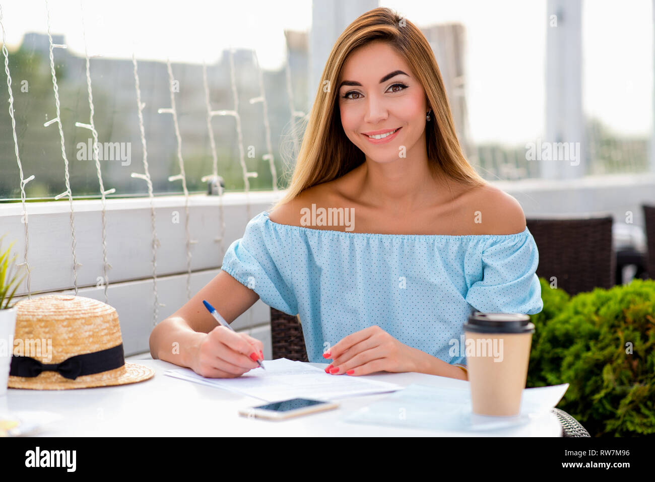 Young beautiful girl signs contract with pen table in summer cafe ...