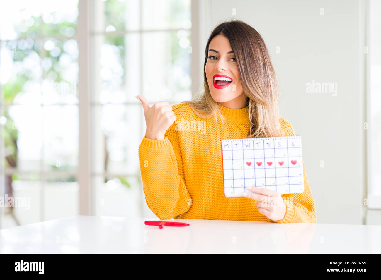 Young beautiful woman holding menstruation calendar at home pointing ...