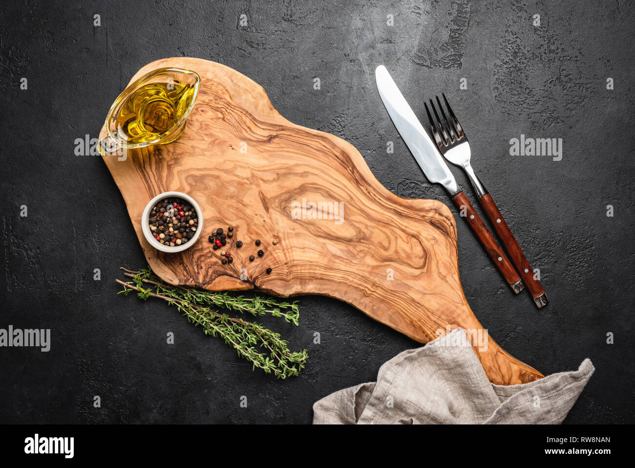 Table setting, eating utensils. Wooden board, cutlery, spices on black ...