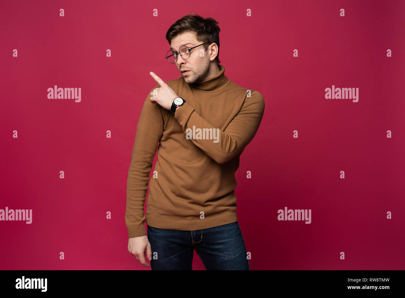 Portrait of a joyful young man pointing fingers away at copy space on ...