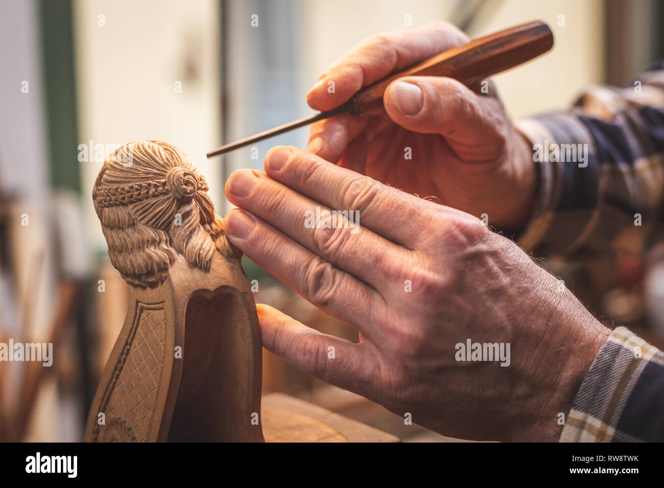 Hands of a wood sculptor with a tool working on a small wooden figure ...