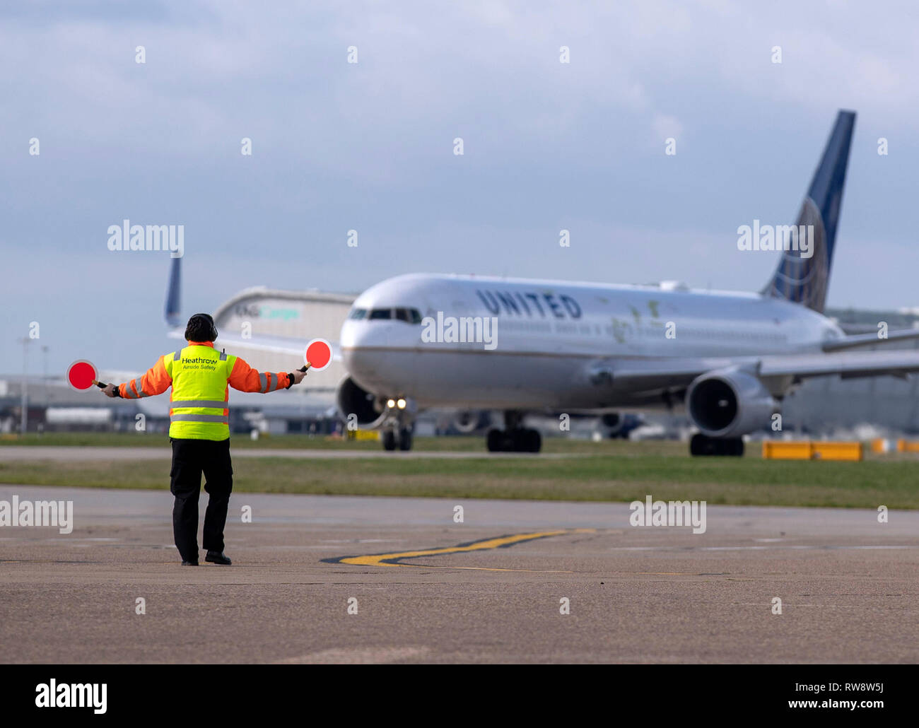 A airside operations member of staff guides in planes at Heathrow ...