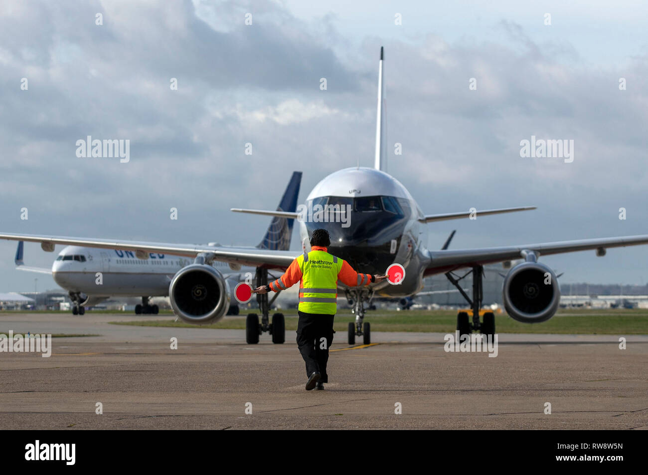A airside operations member of staff guides in planes at Heathrow ...