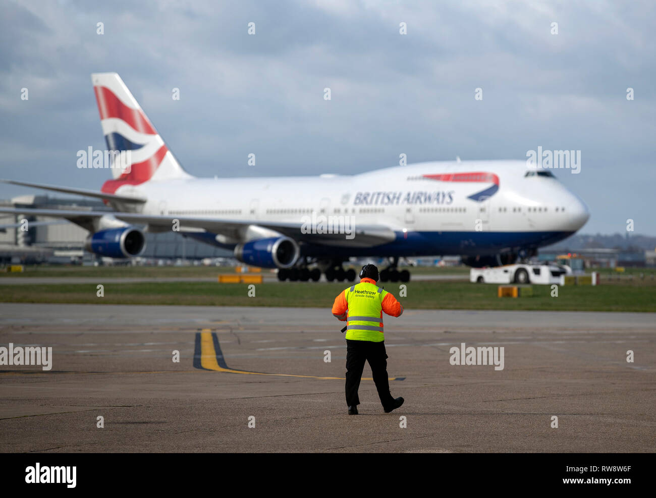 A airside operations member of staff guides in planes at Heathrow ...