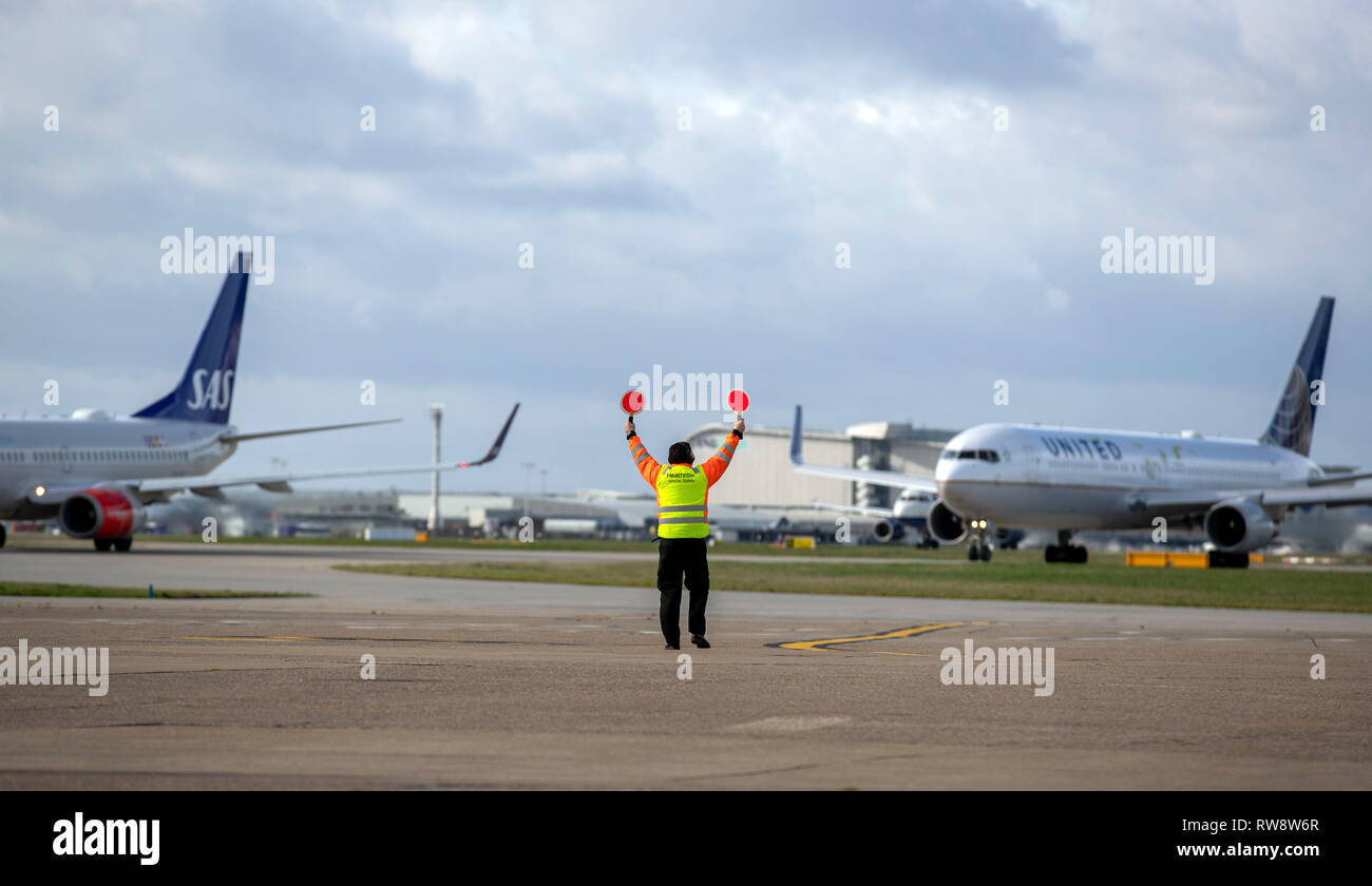 A airside operations member of staff guides in planes at Heathrow ...