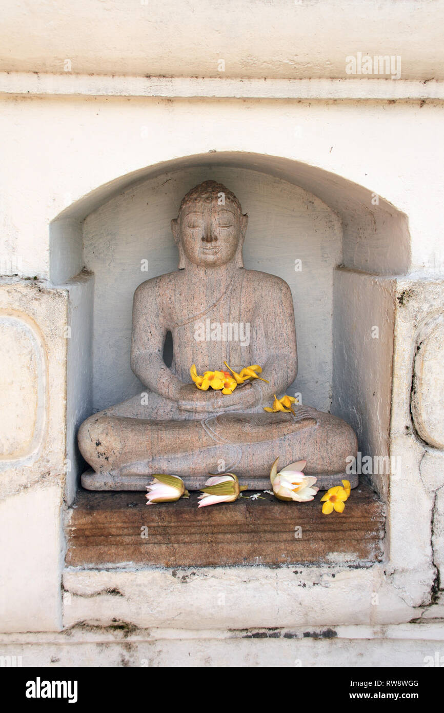 Ancient stone statue of a meditating Buddha with flowers in Isurumuniya ...