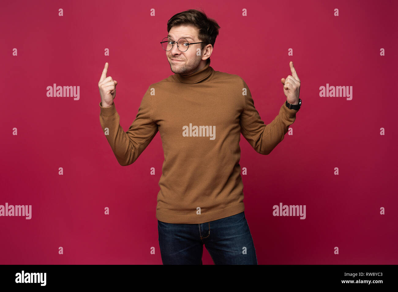 Portrait of a happy young man pointing fingers up at copy space ...