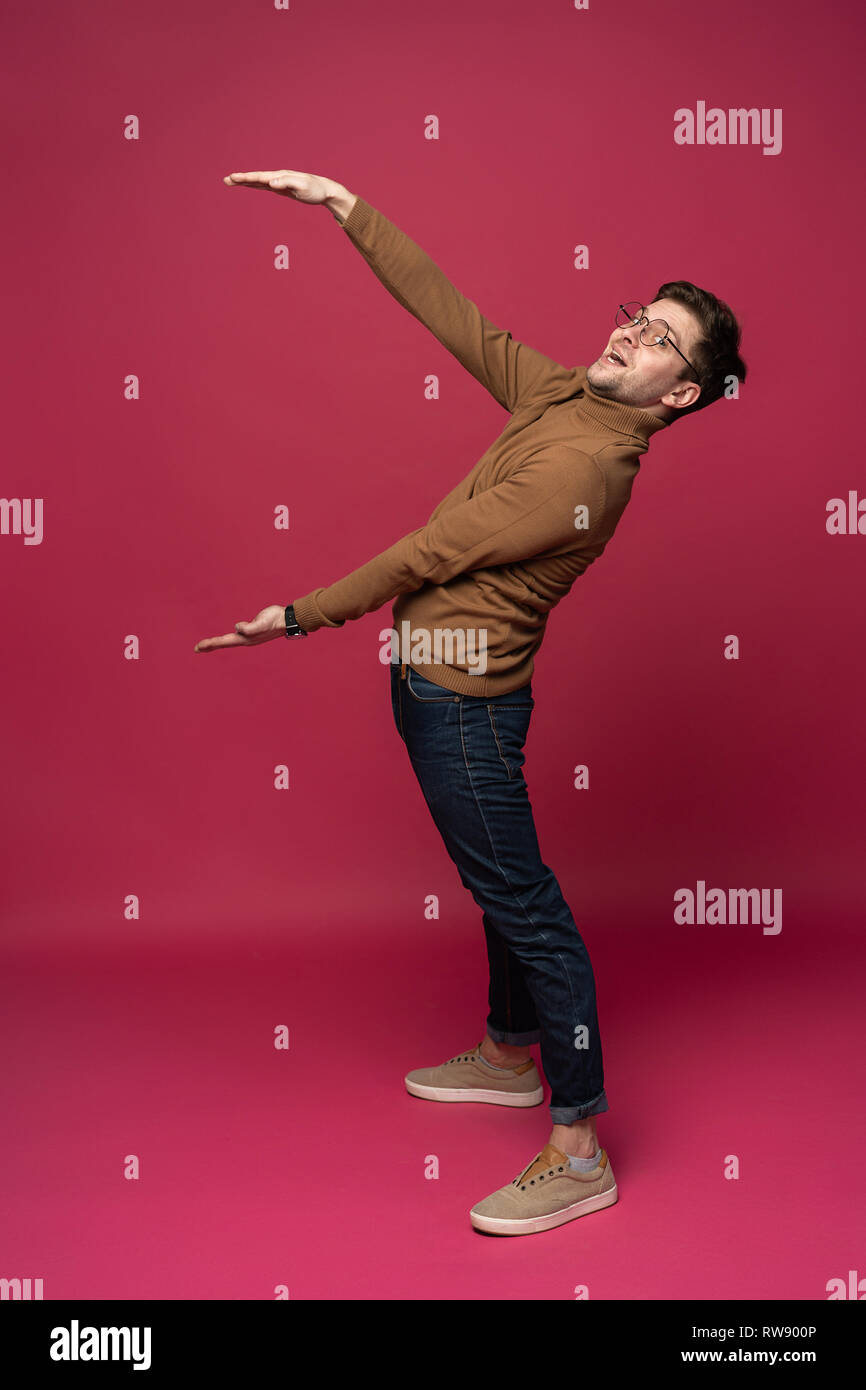 full body picture of a young casual man presenting something on pink ...
