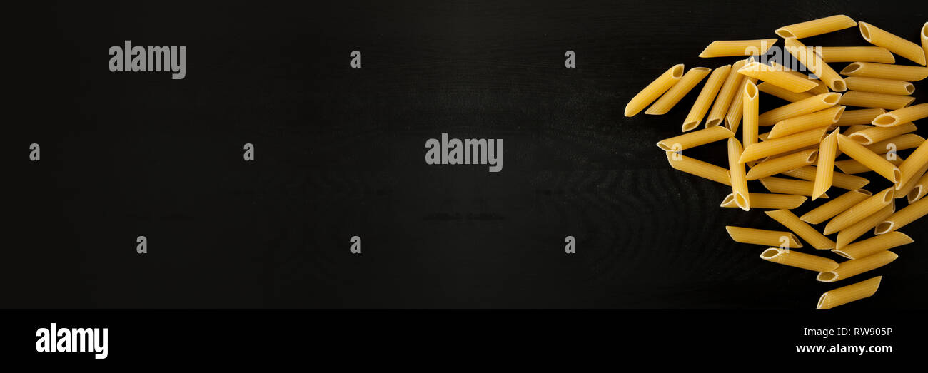 Penne Raw penne italian pasta on a wood black textured background ...