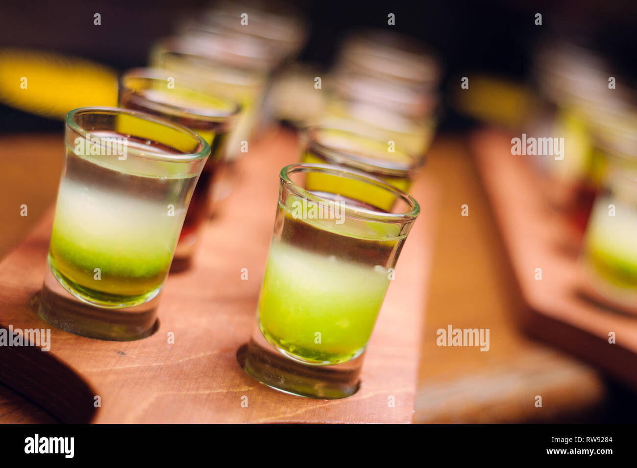 line of alcohol green shots at wooden desk at bar counter. row of ...