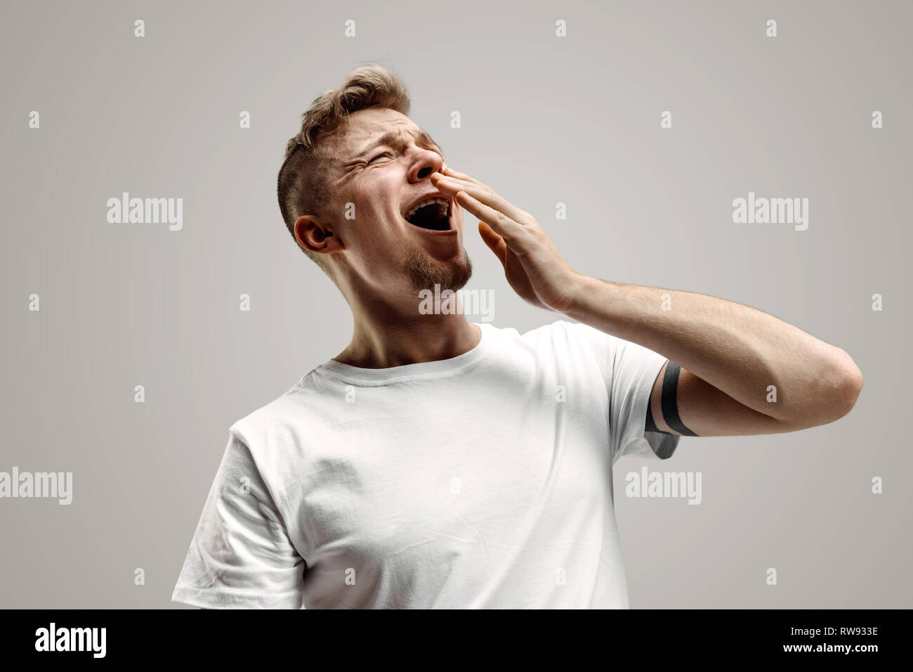 Young man with beard yawning at gray studio background. Human emotions ...