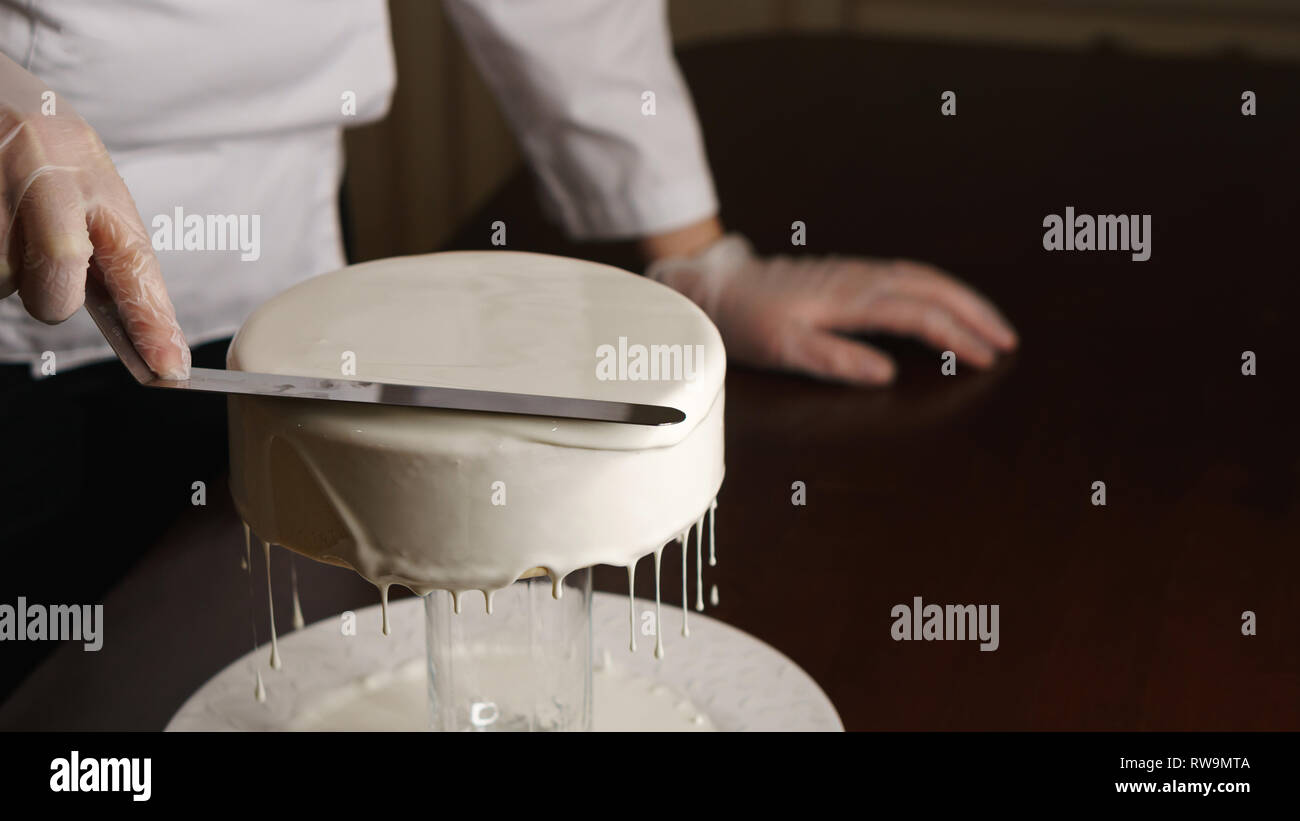 Confectioner fills cakes with white liquid glaze. She equals top ...