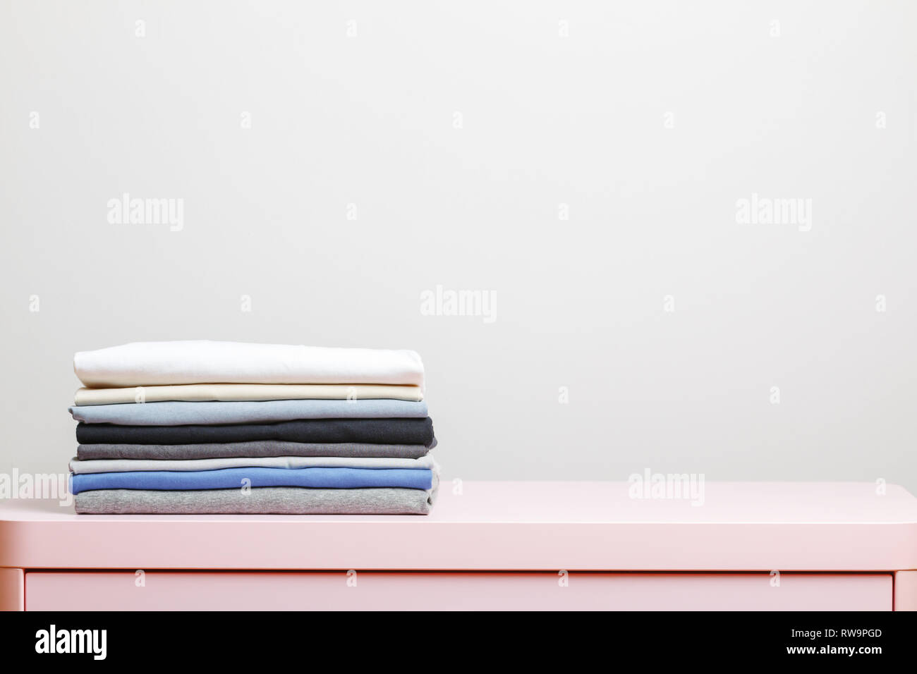 On a pink table is a stack of folded clothes. Gray background. Close-up ...
