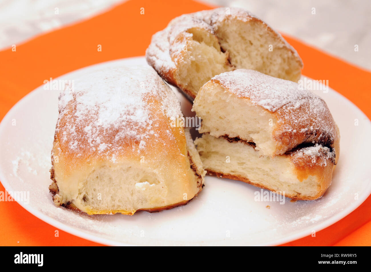 broken bun sprinkled with sugar on a white plate Stock Photo - Alamy