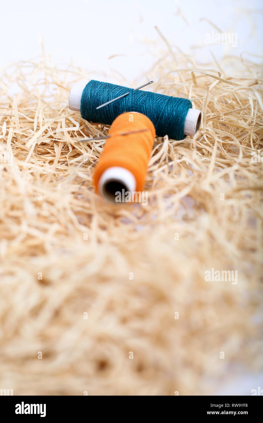 Spool of blue and orange sewing thread with needle on the rafi grass ...