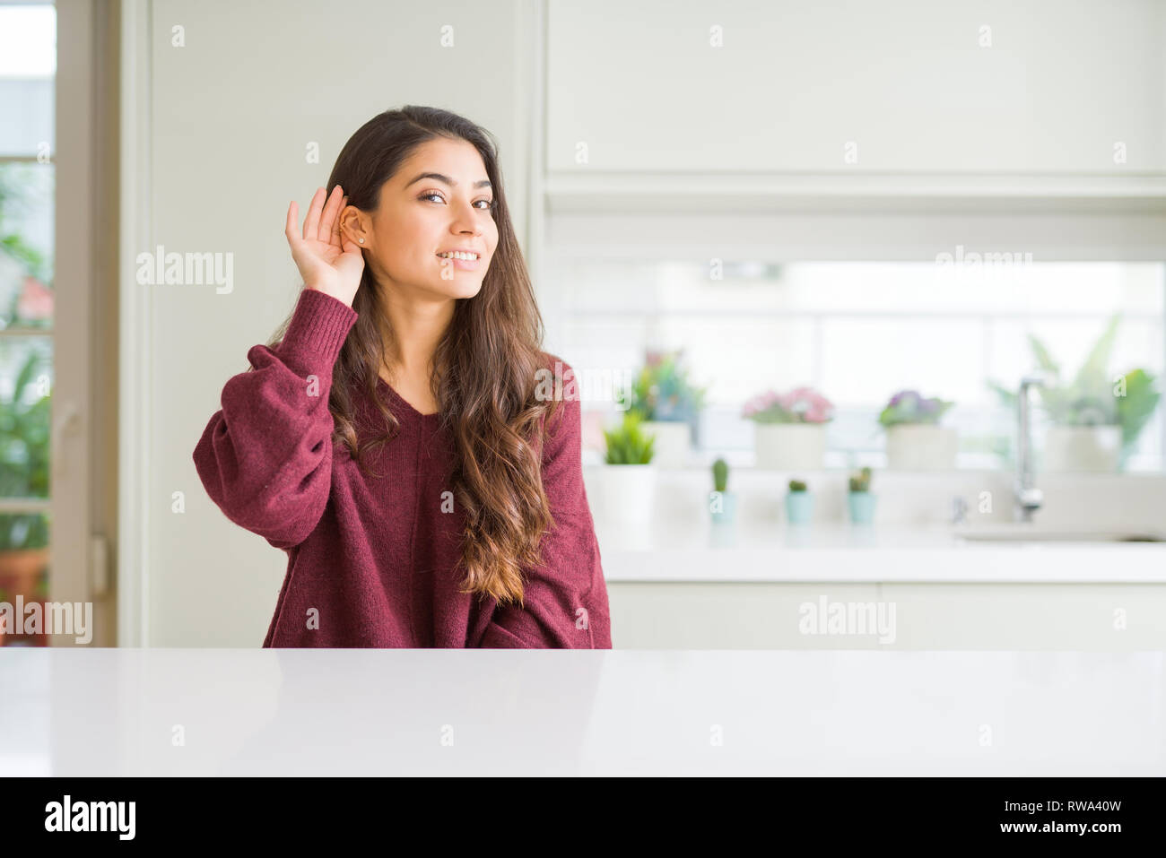 Young beautiful woman at home smiling with hand over ear listening an ...