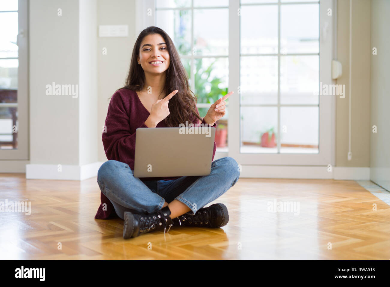 Young woman using computer laptop sitting on the floor smiling and ...