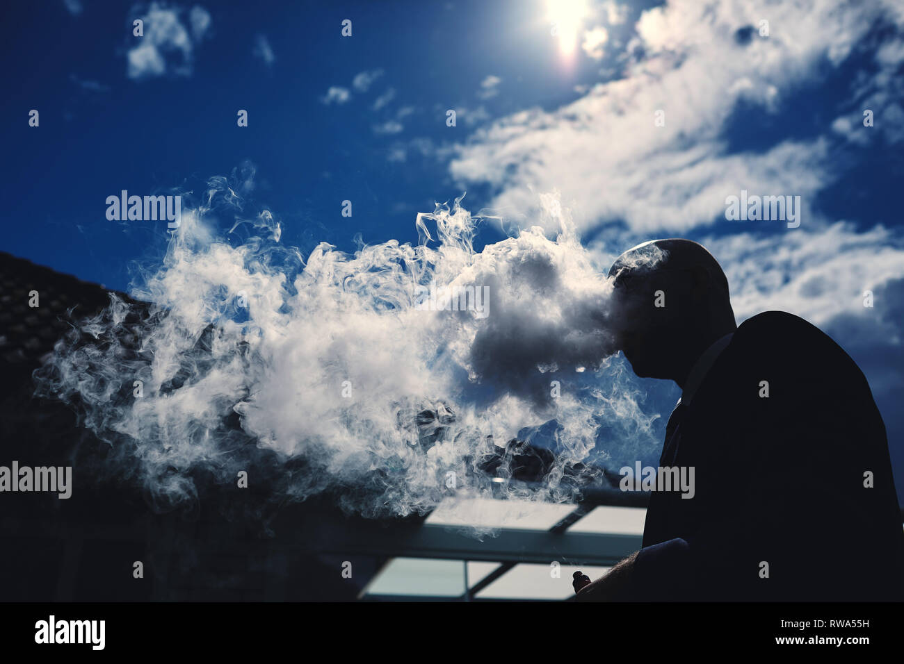 A man smokes a cigarette and releases a lot of smoke into the air Stock ...