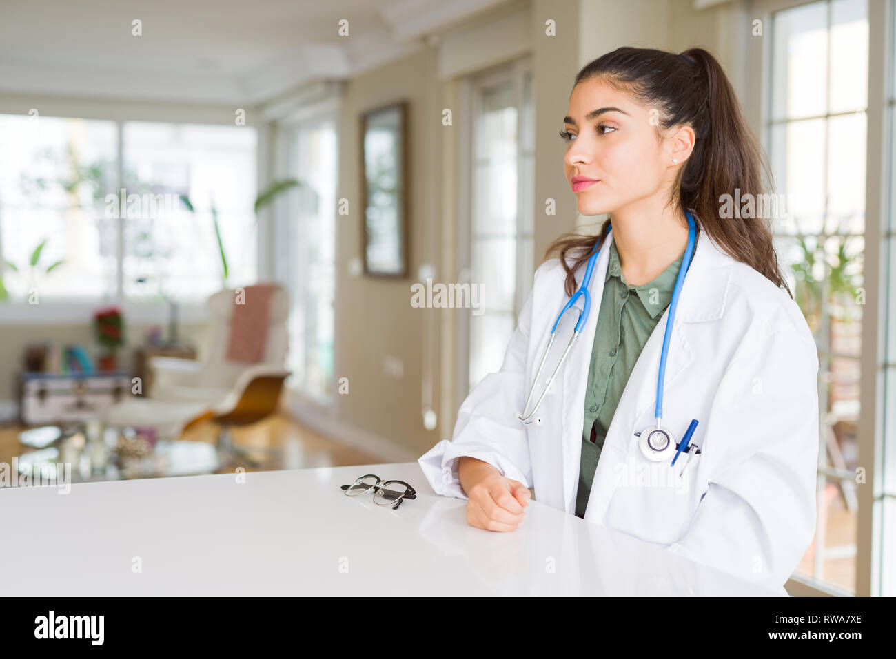Young doctor woman wearing medical coat at the clinic looking to side ...