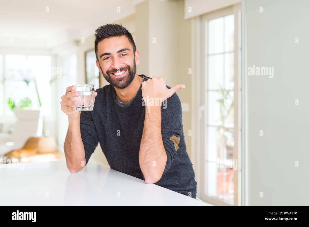 Handsome hispanic man drinking a fresh glass of water pointing and ...