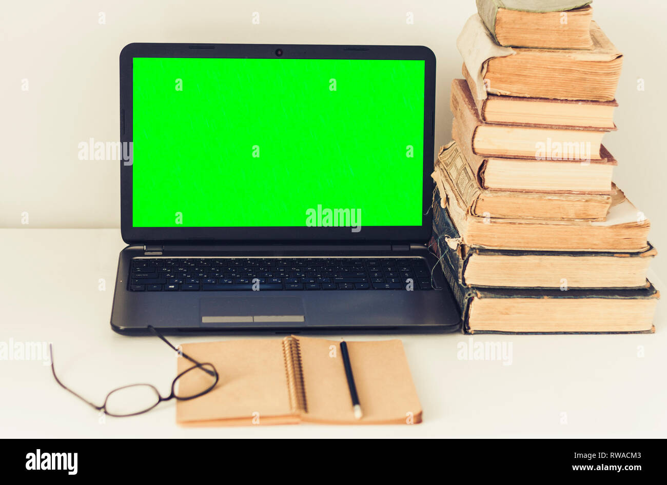 Green screen laptop, stack of old books, notebook and pencils on white ...