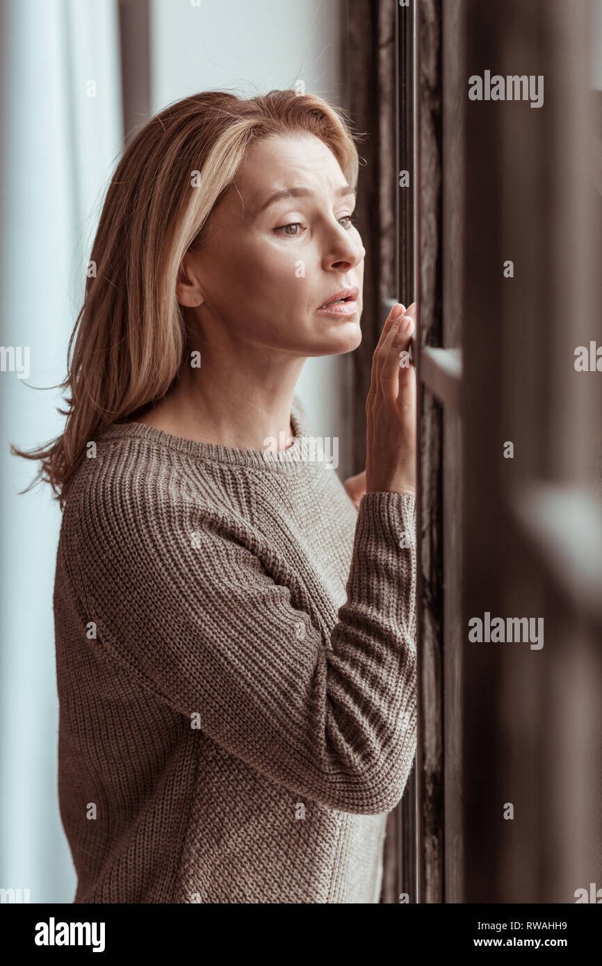 Mature woman looking into window and feeling stressed Stock Photo - Alamy