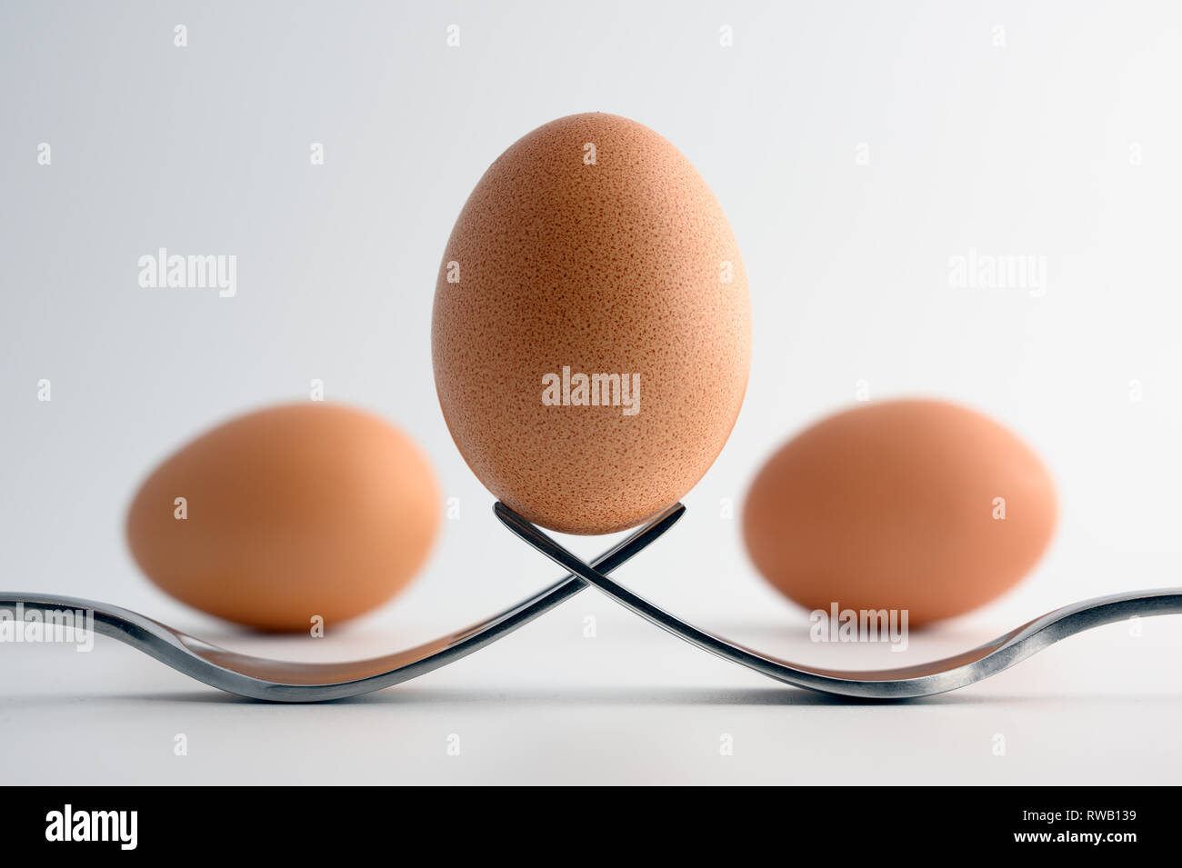 Egg in balance on two forks on white background. Two more eggs out of ...