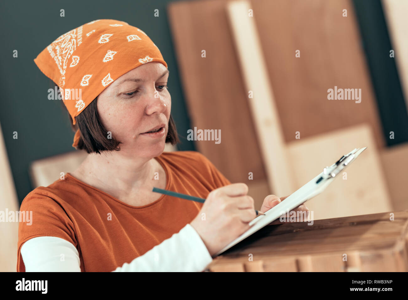 Female carpenter writing DIY project notes after finishing wooden crate ...