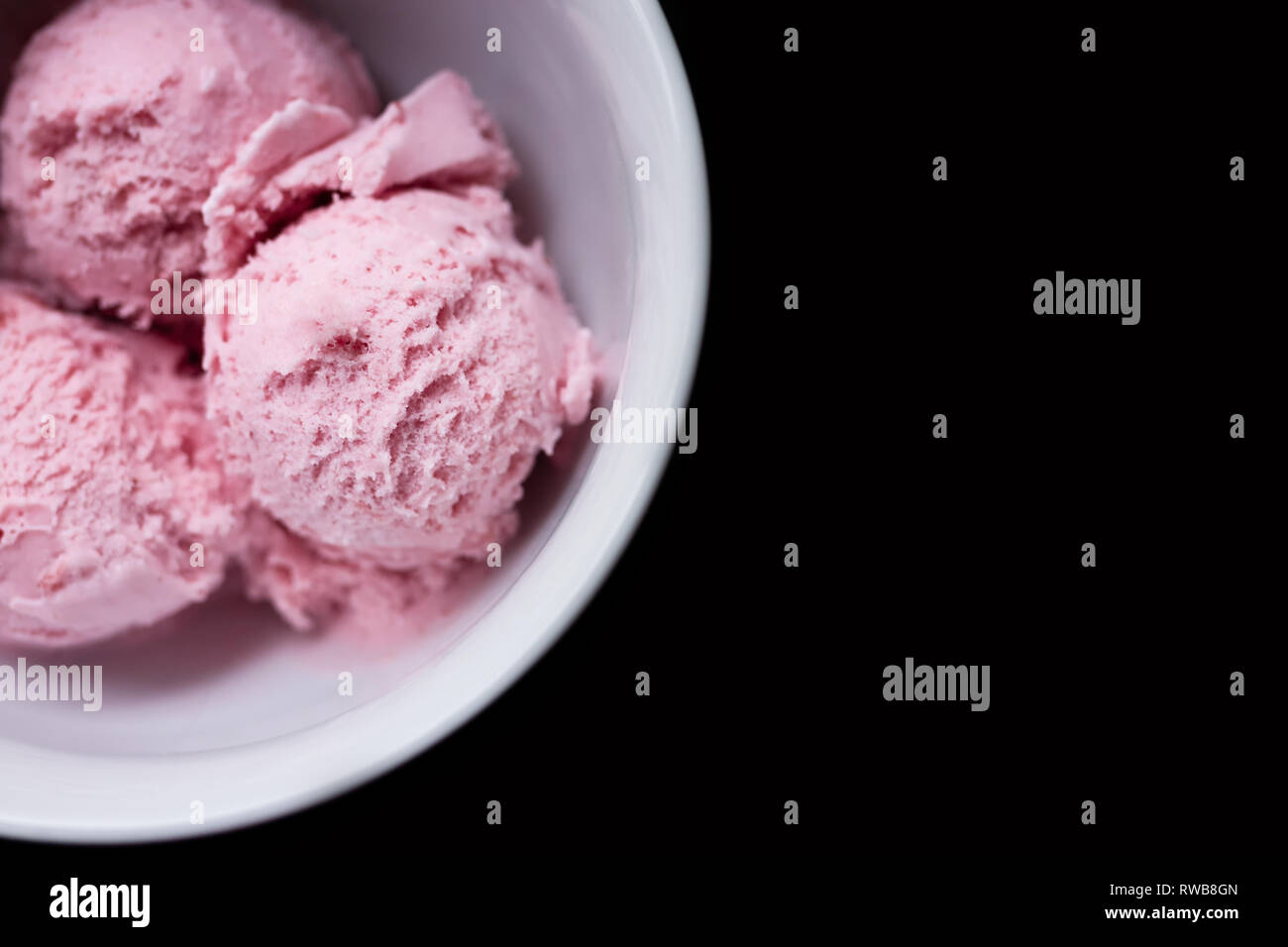 Three scoops of pink strawberry ice cream in white bowl on black ...