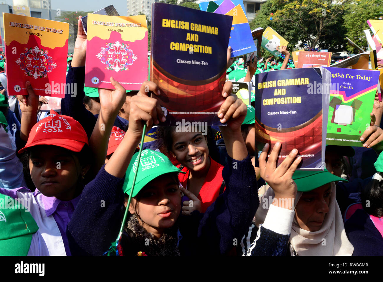 Bangladeshi students raise their books received at a distribution event ...