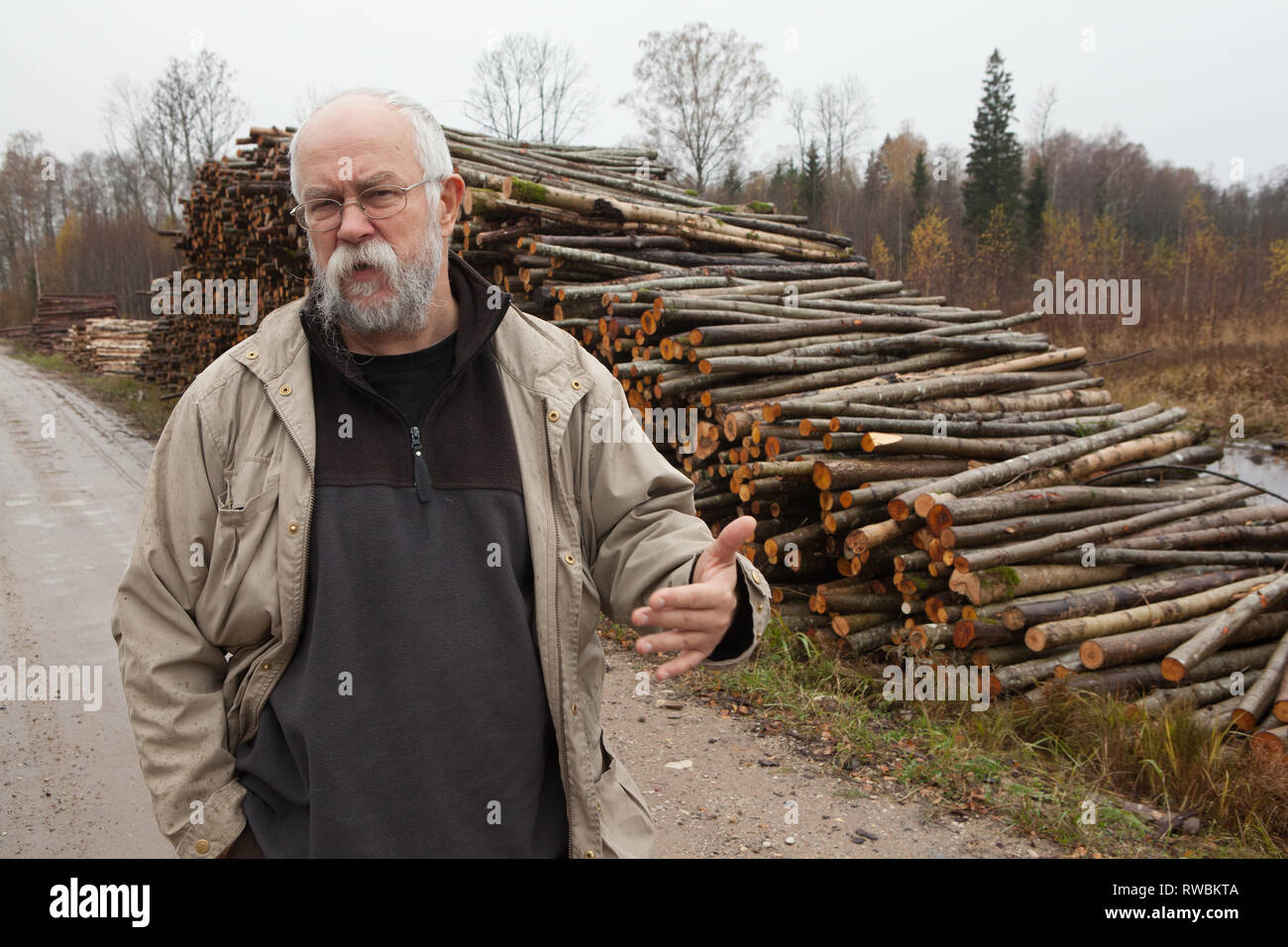 Man on dirt track next to stacked forest clearance tree trunks on ...