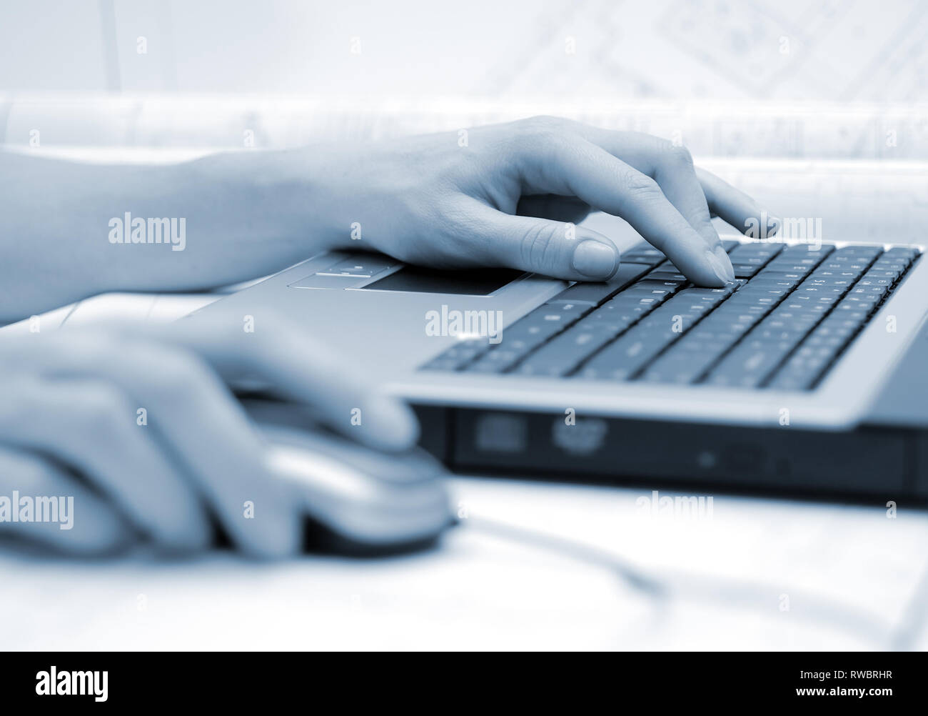 Female hands on laptop keyboard. Architectural plans in background ...