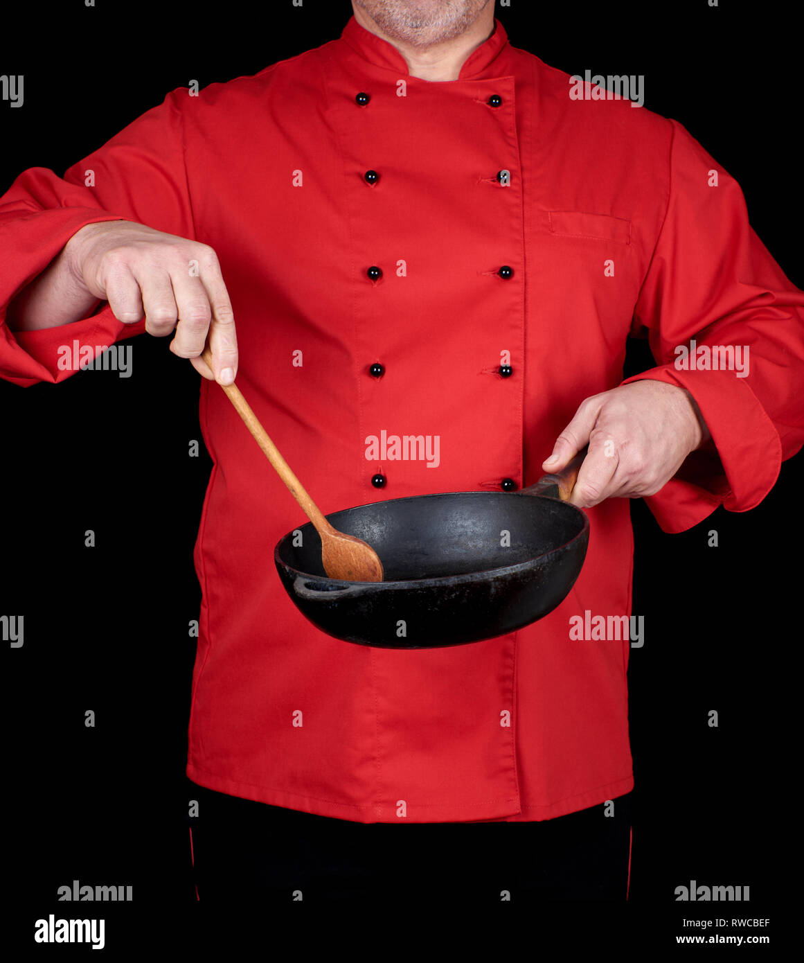 cook in red uniform holding an empty black frying pan and wooden spoon ...
