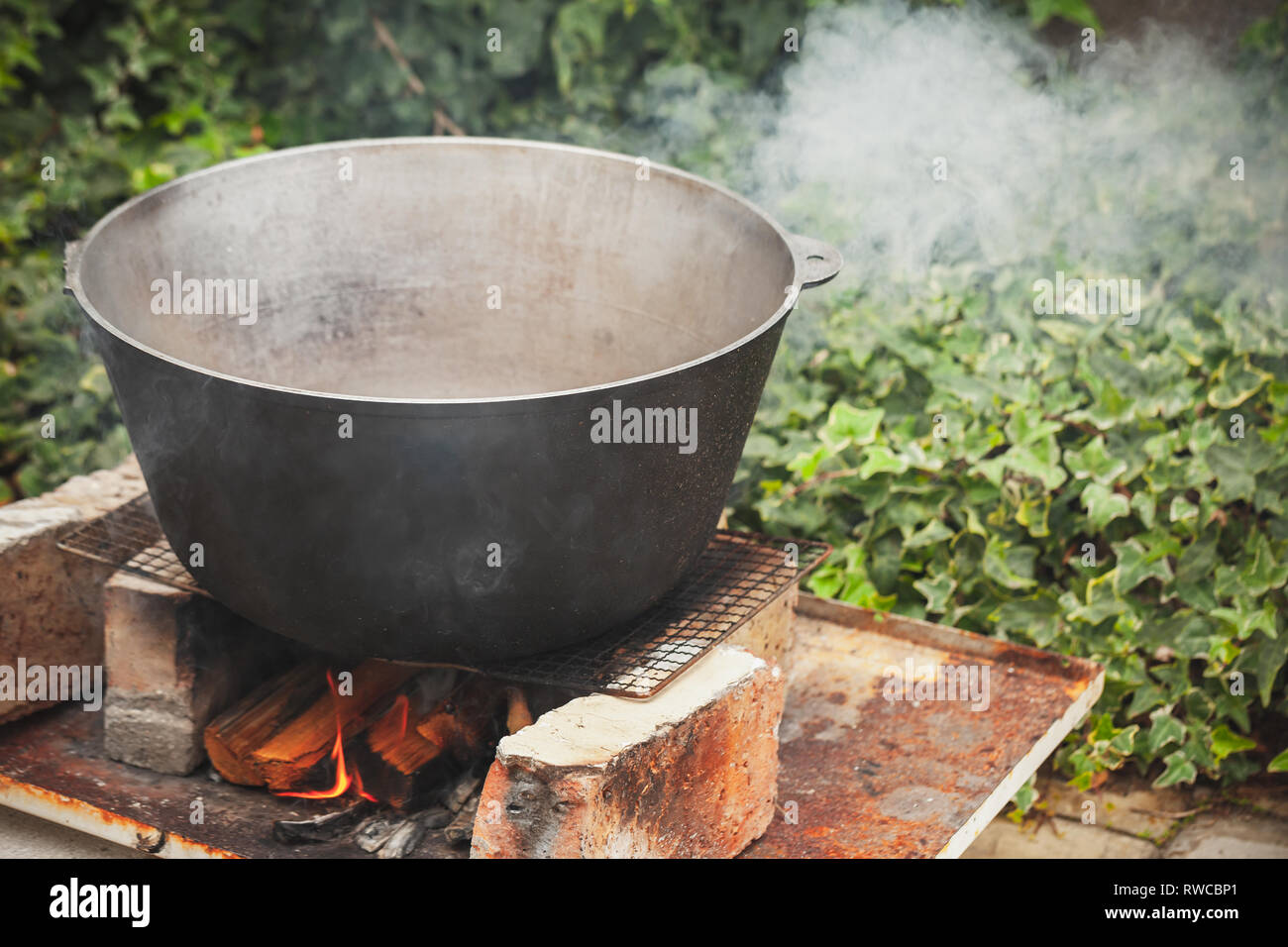 Black cauldron with steam is on a bonfire. Outdoor preparing of Chorba ...
