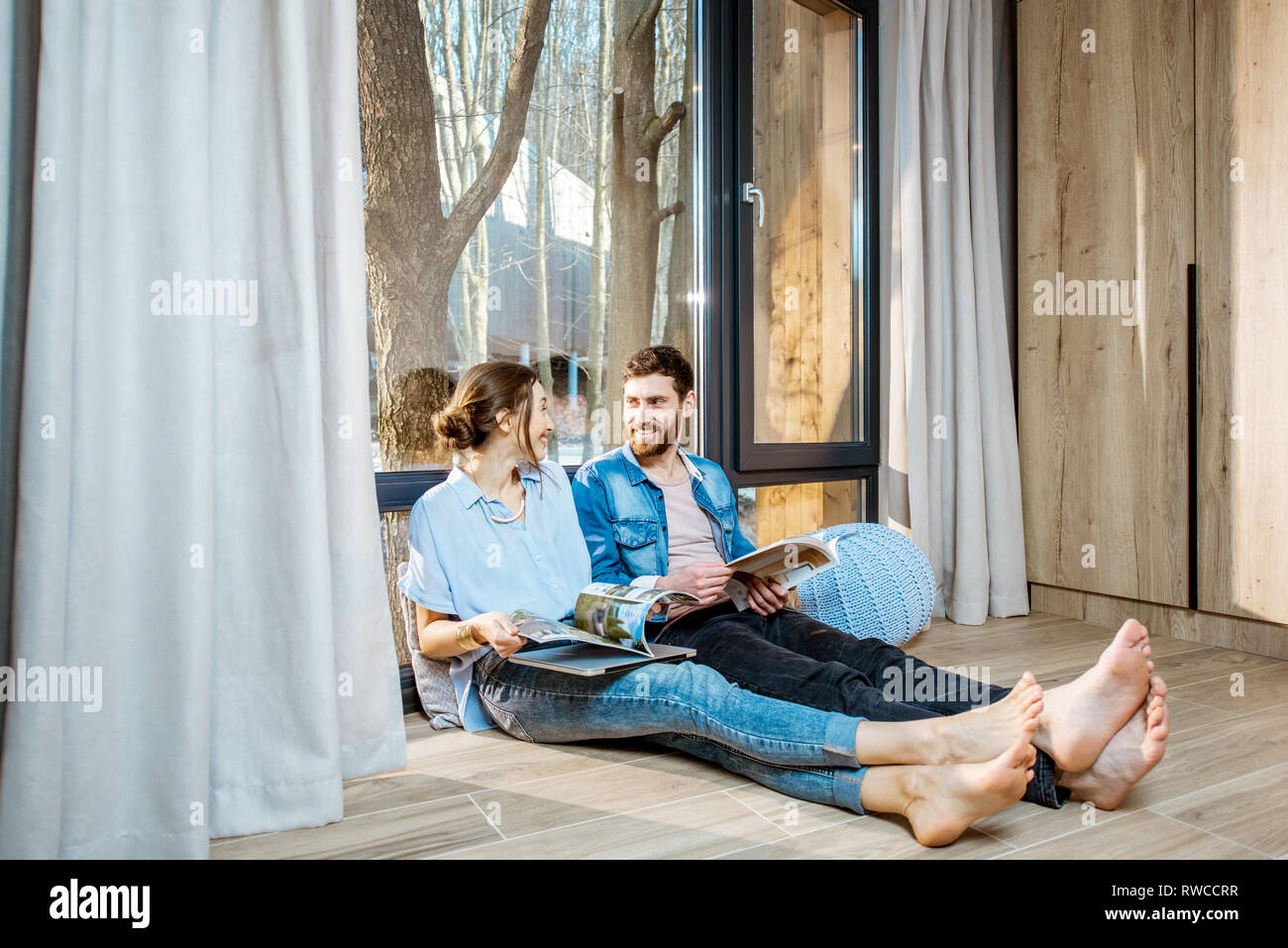 Happy couple sitting together on the floor near the window with ...