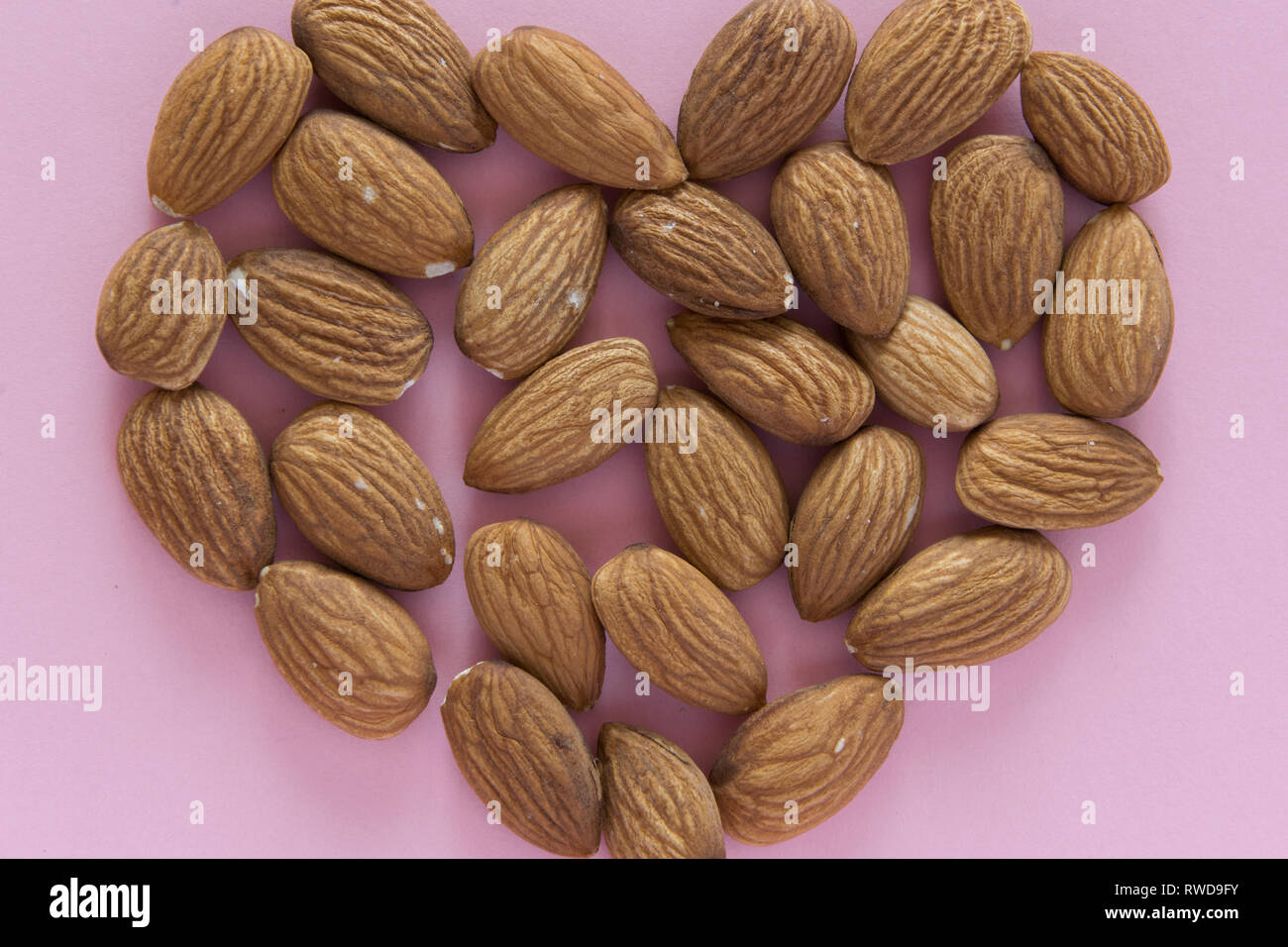 Top view of raw almonds in heart shape on pink background Stock Photo ...