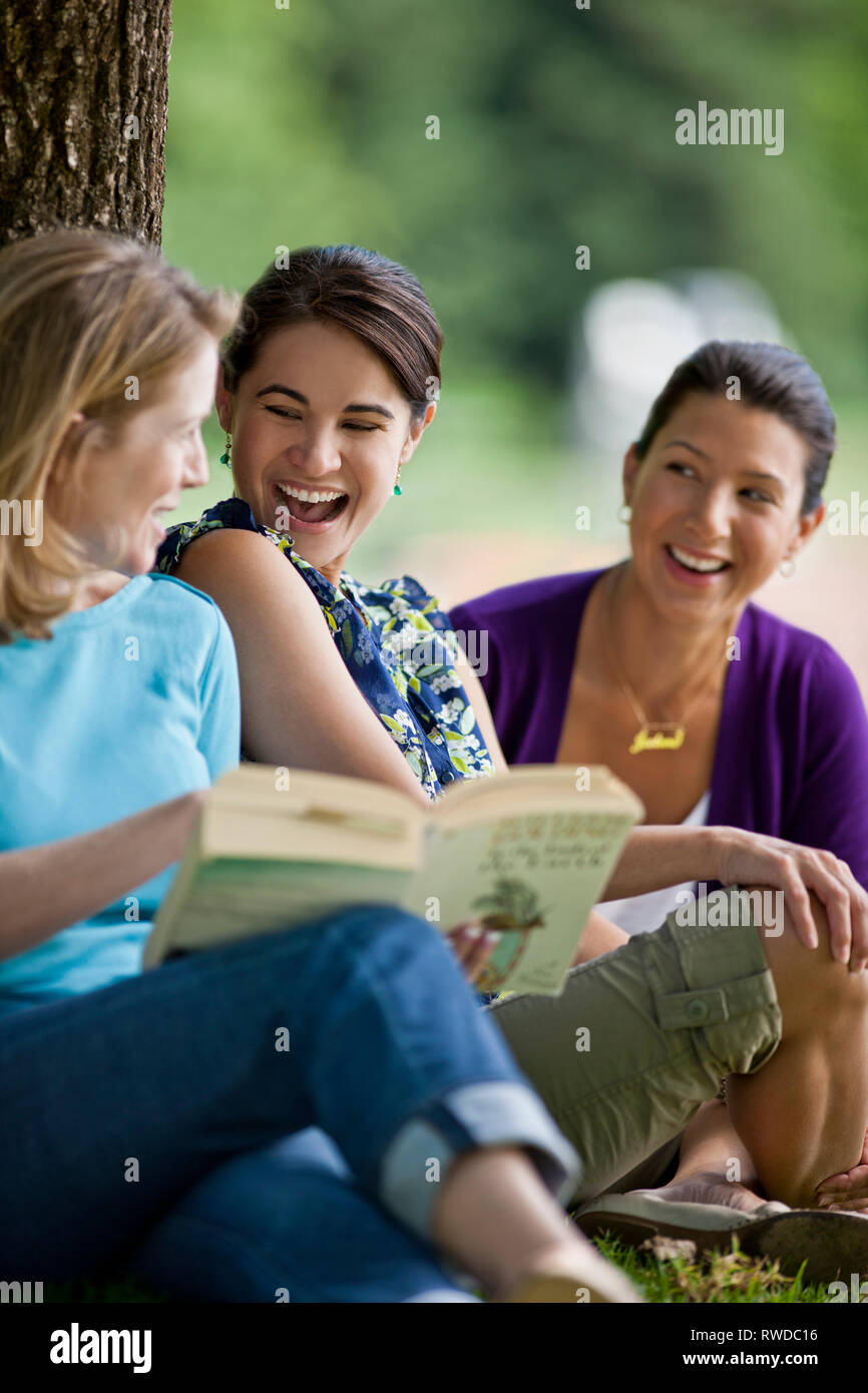 Happy friends reading a book together under a tree at the park Stock ...