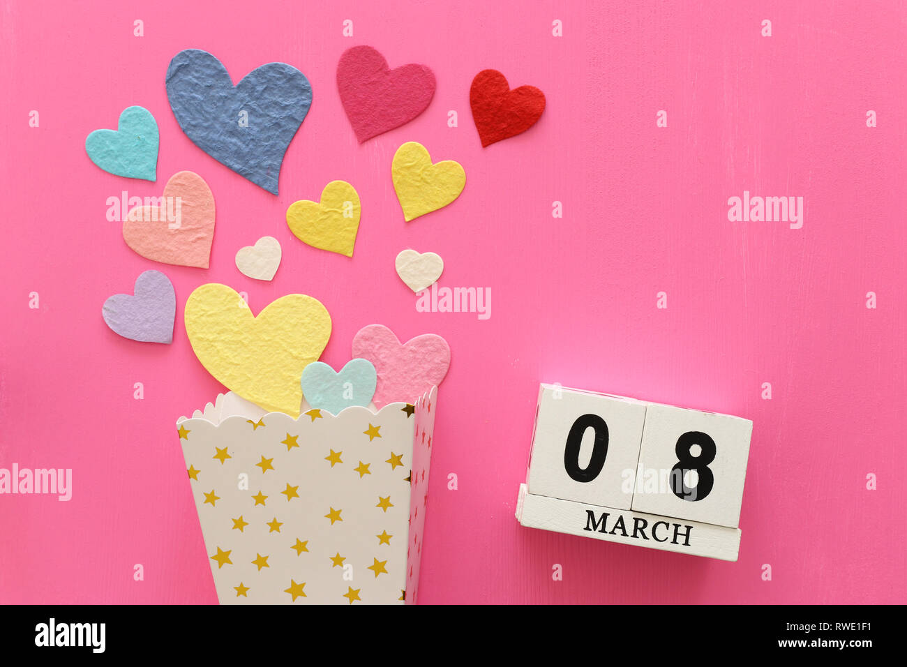 wooden March 8 calendar next to paper colorful hearts over pink wooden ...