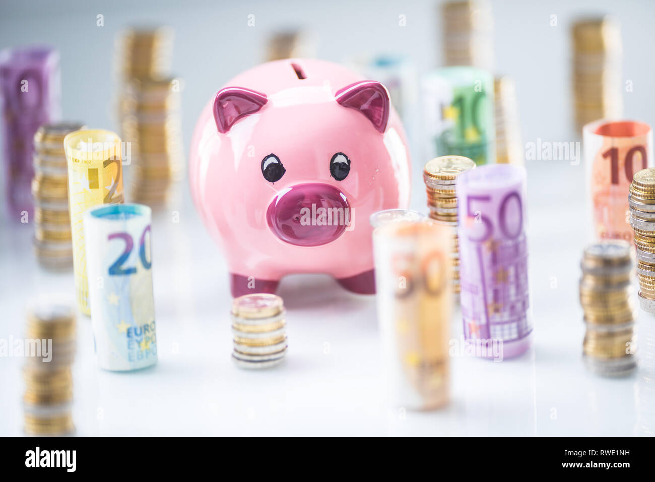 Pink piggy bank in the middle of rolled euro banknotes and towers with ...