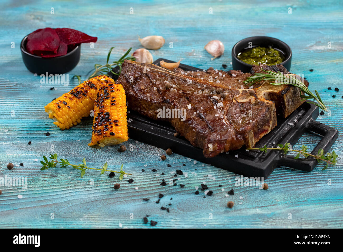 T-bone beef stake served on a cutting board with sauces, rosemary, corn ...