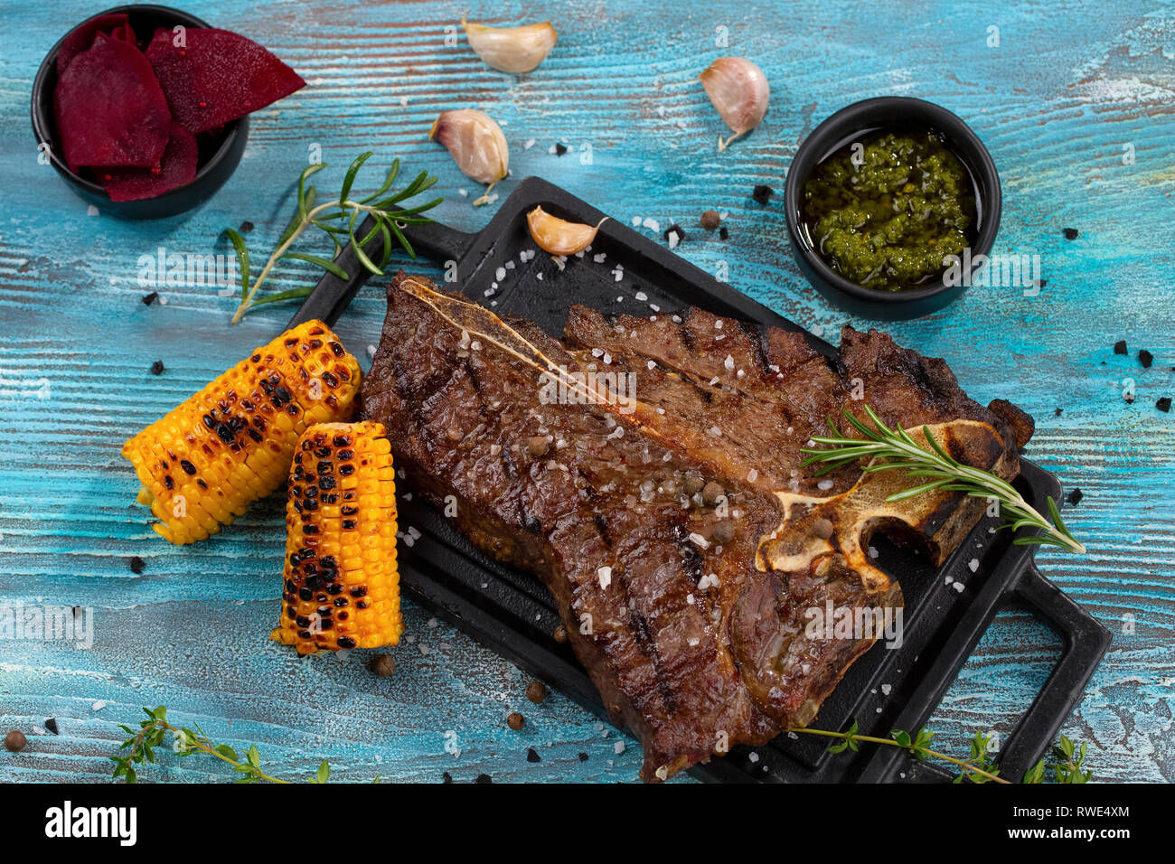 T-bone beef stake served on a cutting board with sauces, rosemary, corn ...