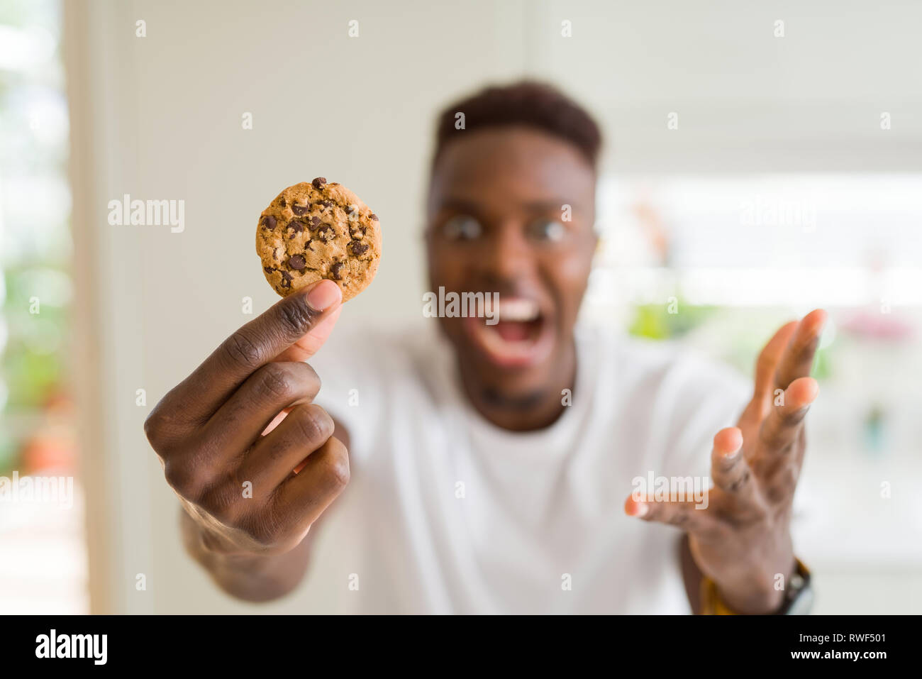 Young african american man eating chocolate chips cookies very happy ...