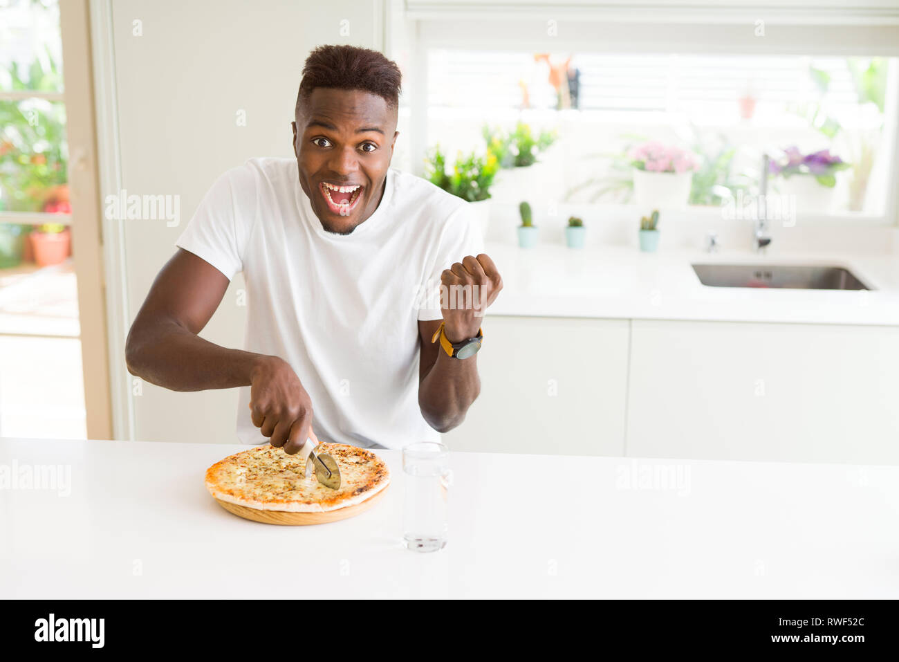 African american man eating cheese pizza at home screaming proud and ...