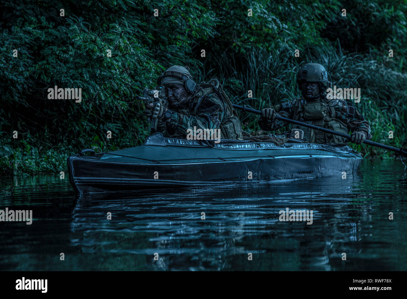Special forces men paddling Army kayak across the river at twilight ...