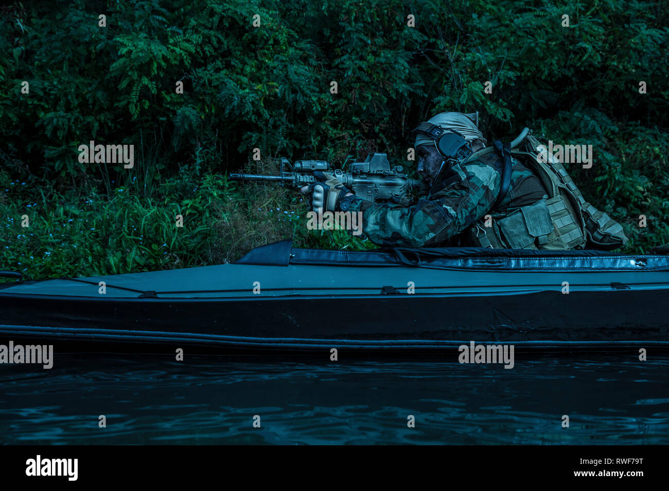 Special forces men paddling Army kayak across the river at twilight ...