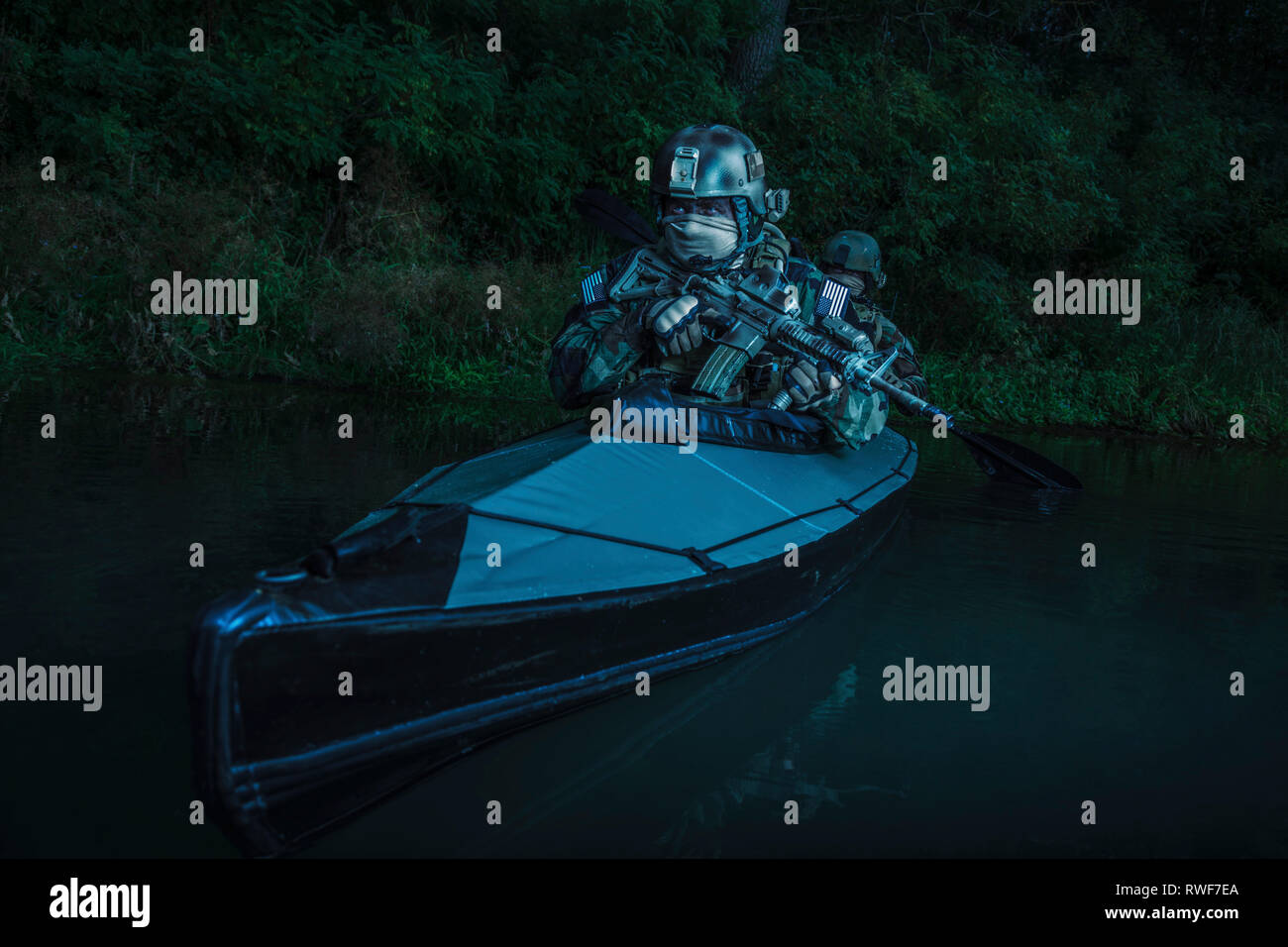 Special forces men paddling Army kayak across the river at twilight ...