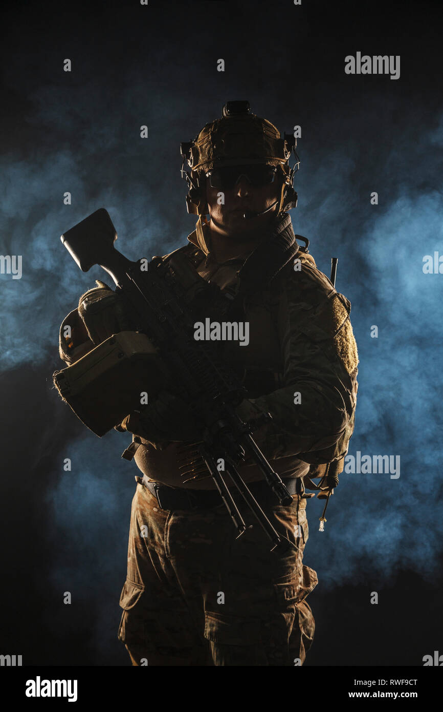 Army soldier in combat uniform with machine gun, dark smoke background ...