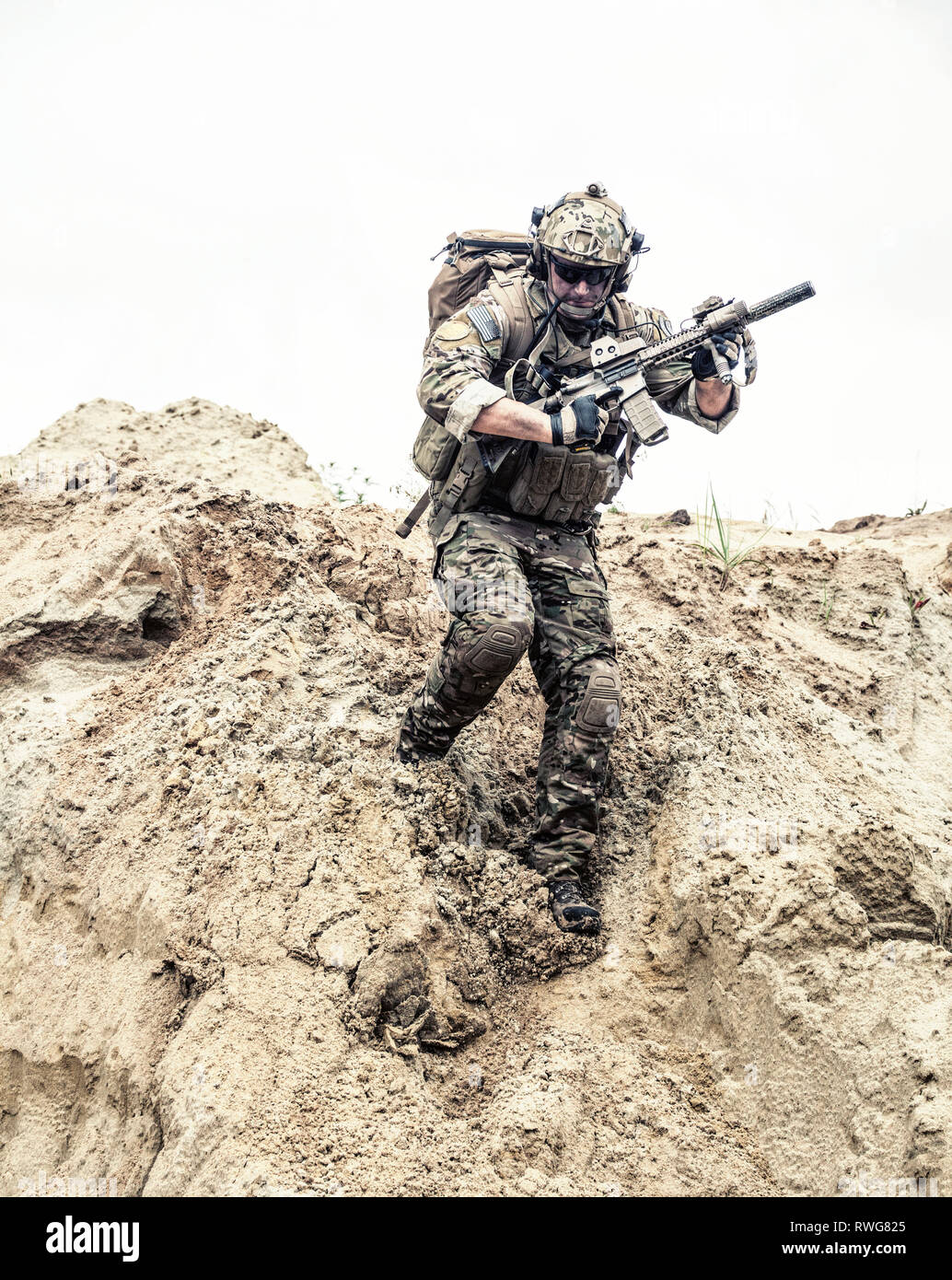 U.S. Army commando moving down a steep sand dune with his assault rifle ...